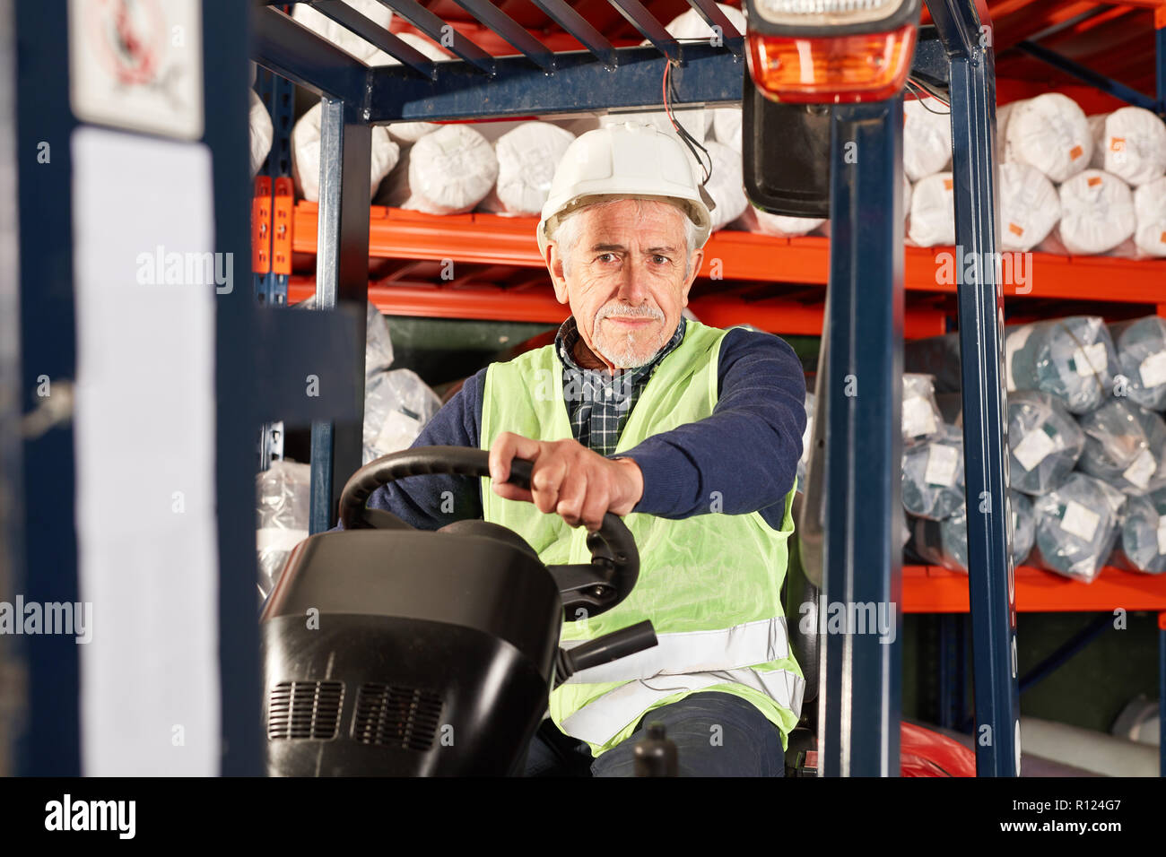 Senior worker on the forklift in a warehouse of a logistics company ...