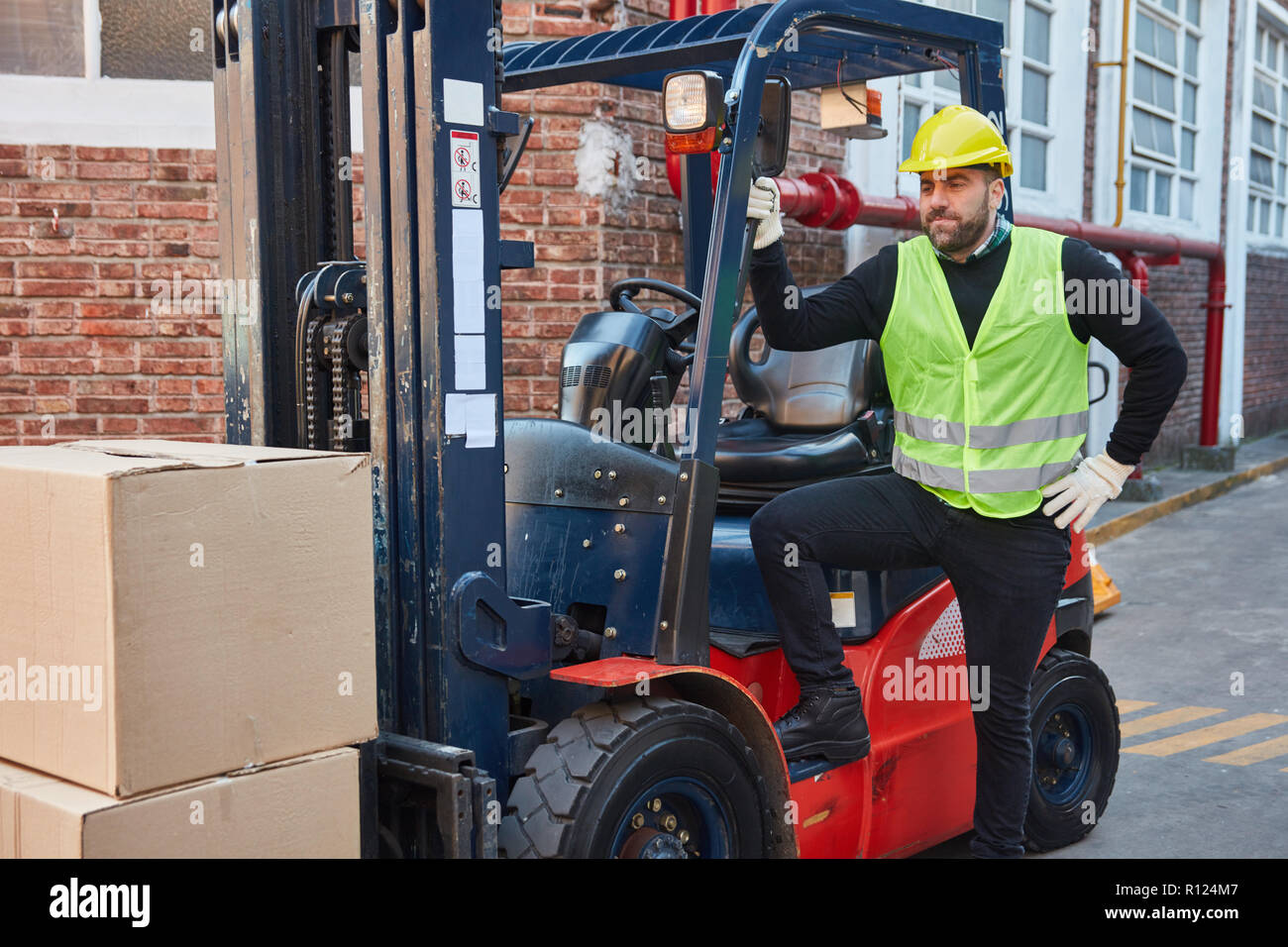 Man as a forklift driver stands in front of his forklift with packages ...
