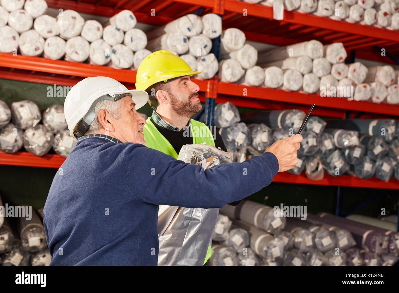 Two warehouse workers work together in the carpet warehouse of a ...