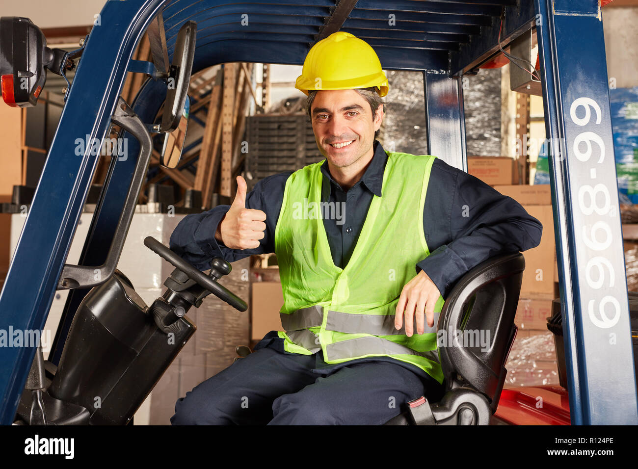 Young warehouse worker with thumbs up as a stacker driver in a ...