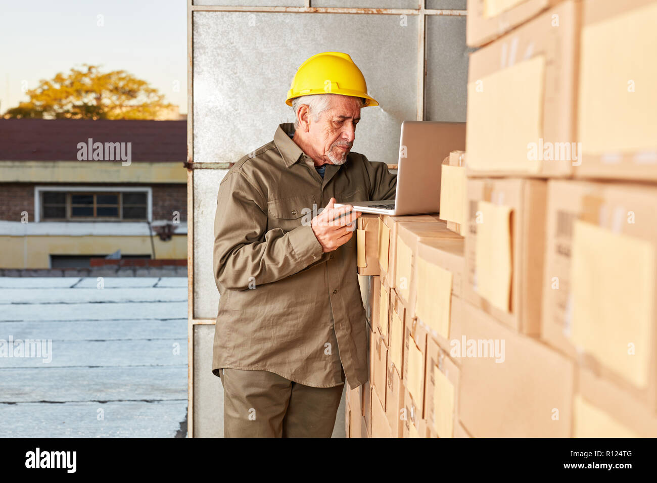 Senior as warehouse specialist with computer in warehouse with packages ...