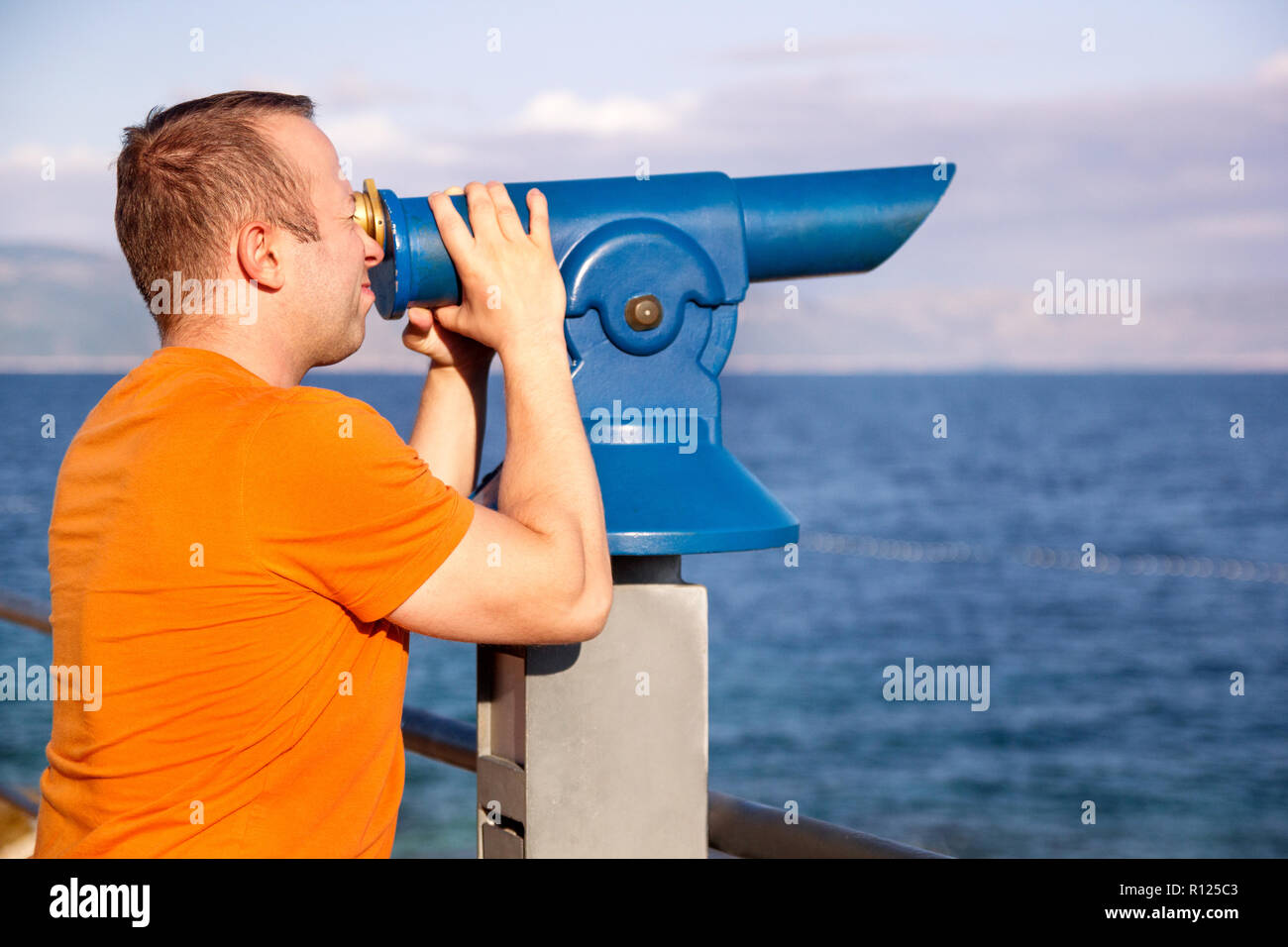 Tourist watches beautiful natural environment in telescope on beach ...