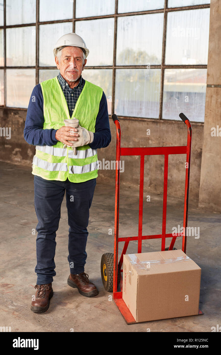 Senior as a warehouse worker with a sack truck carries a package as a ...
