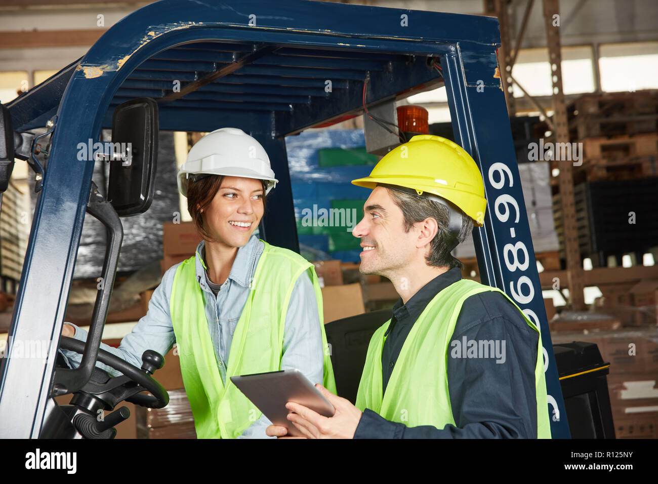 Warehouse worker and woman on forklift work as a team in warehouse ...