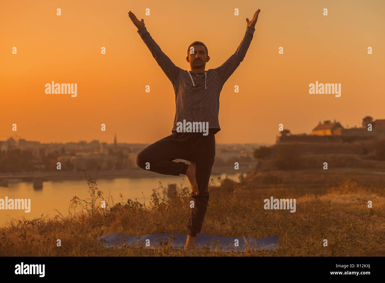 Man doing yoga on sunset with city view,Tree pose/Vrikshasana.Toned ...