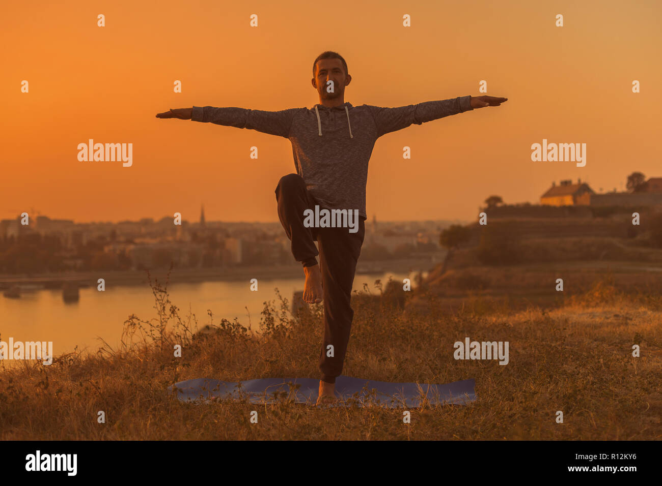 Man doing yoga on sunset with city view,Tree pose/Vrikshasana.Toned ...