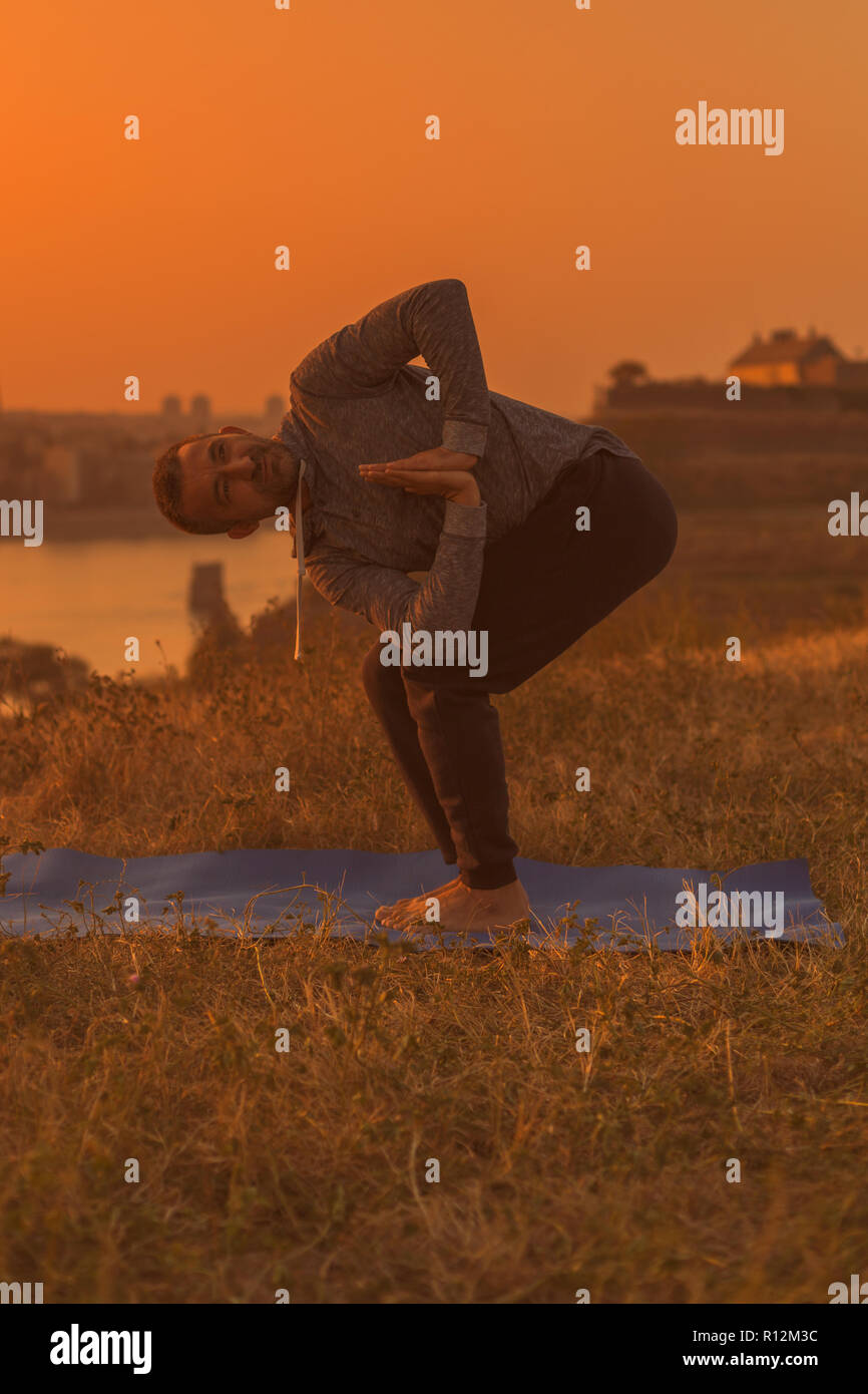 Man doing yoga on sunset with city view, Revolved Chair Pose /Parivrtta ...