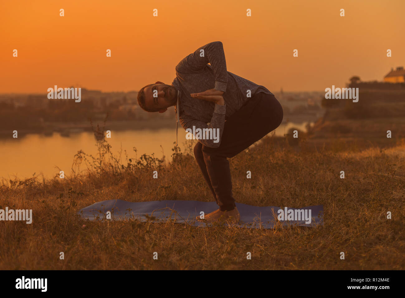 Man doing yoga on sunset with city view, Revolved Chair Pose /Parivrtta ...