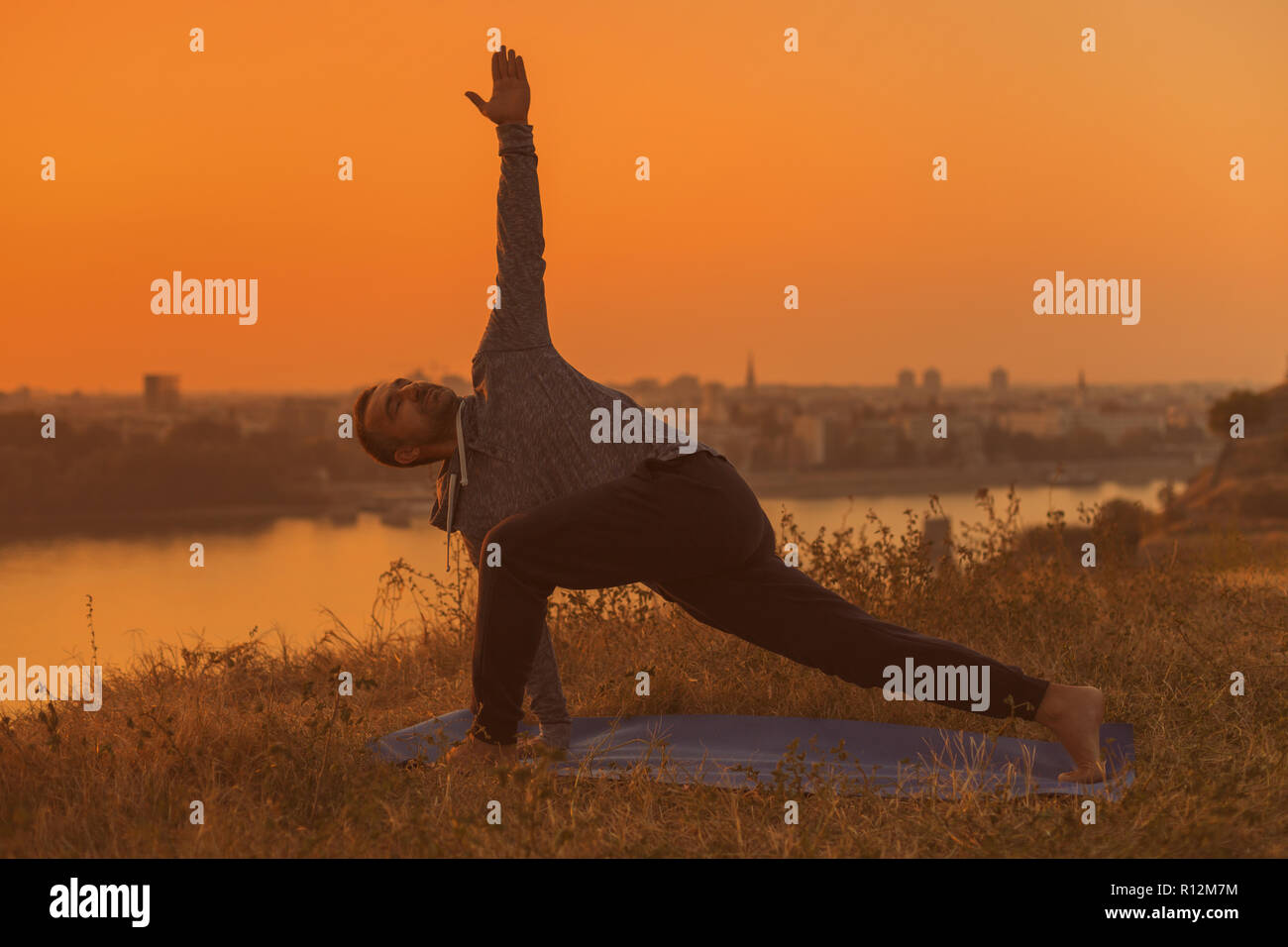 Man doing yoga on sunset with city view,Trikonasana /Triangle pose ...