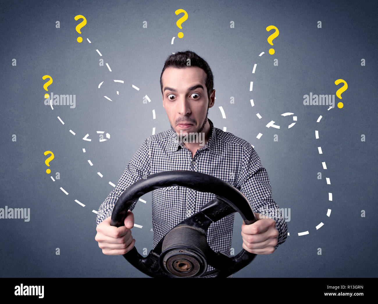 Young man holding black steering wheel with question marks around him ...