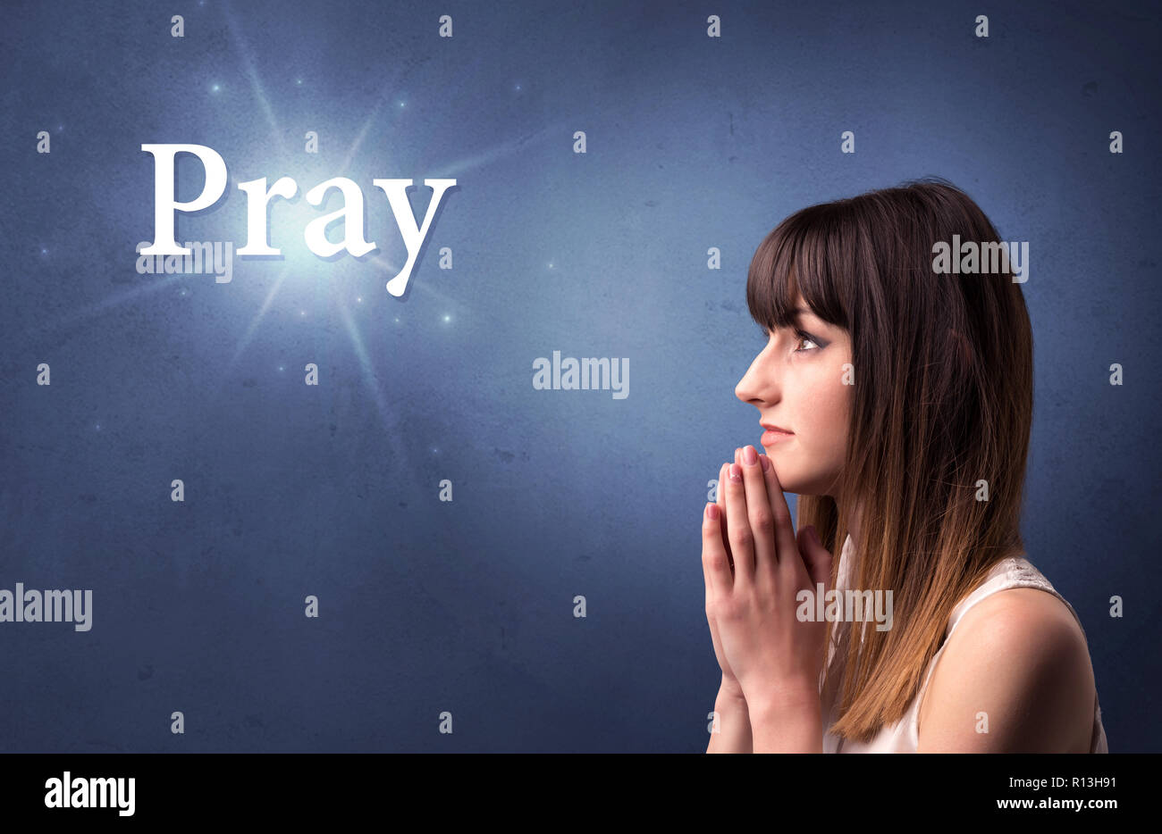 Young woman praying on a blue background with the word Pray written ...