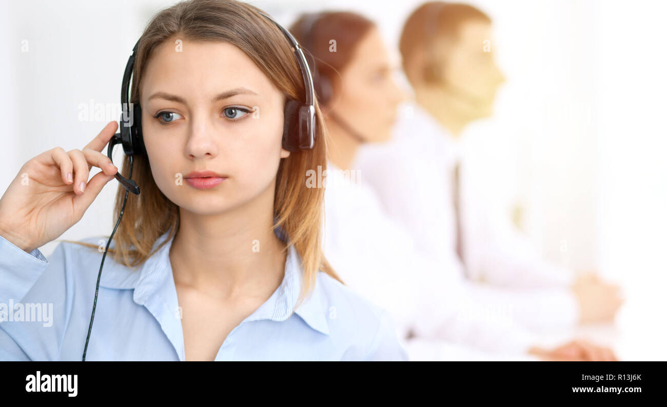 Call center operators. Focus on young cheerful smiling woman in headset. Business and customer ...