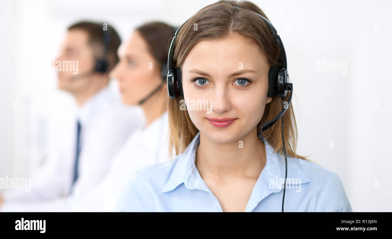 Call center operators. Focus on young cheerful smiling woman in headset. Business and customer ...