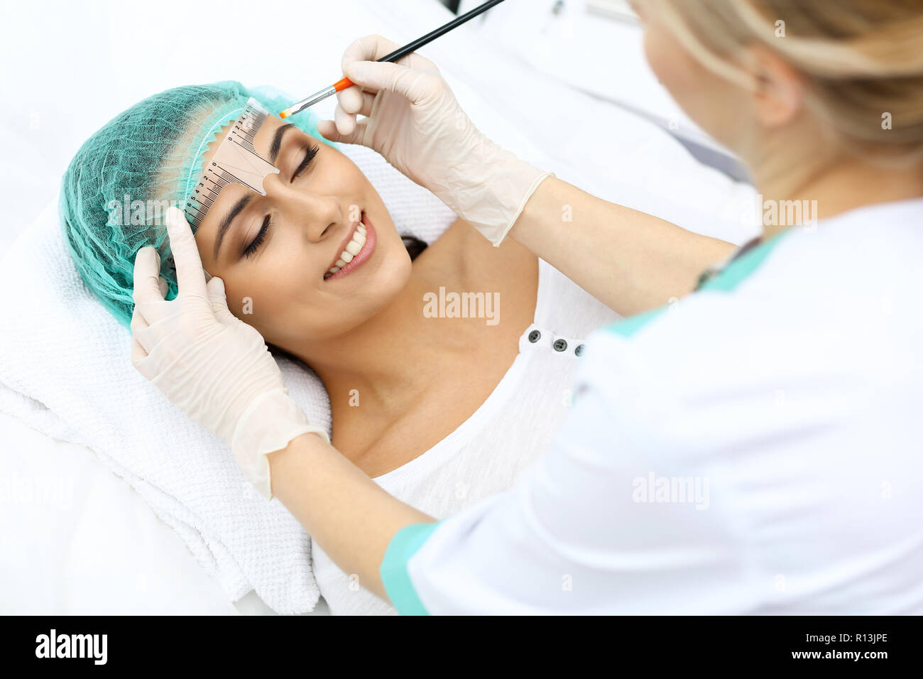 Professional beautician is going to correct eyebrow line at woman face ...