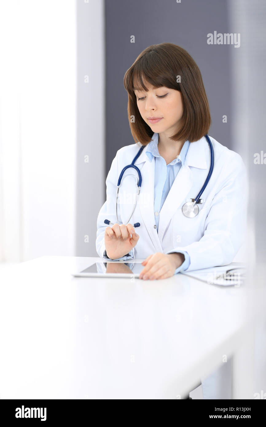 Female doctor typing on laptop computer while sitting at the white ...