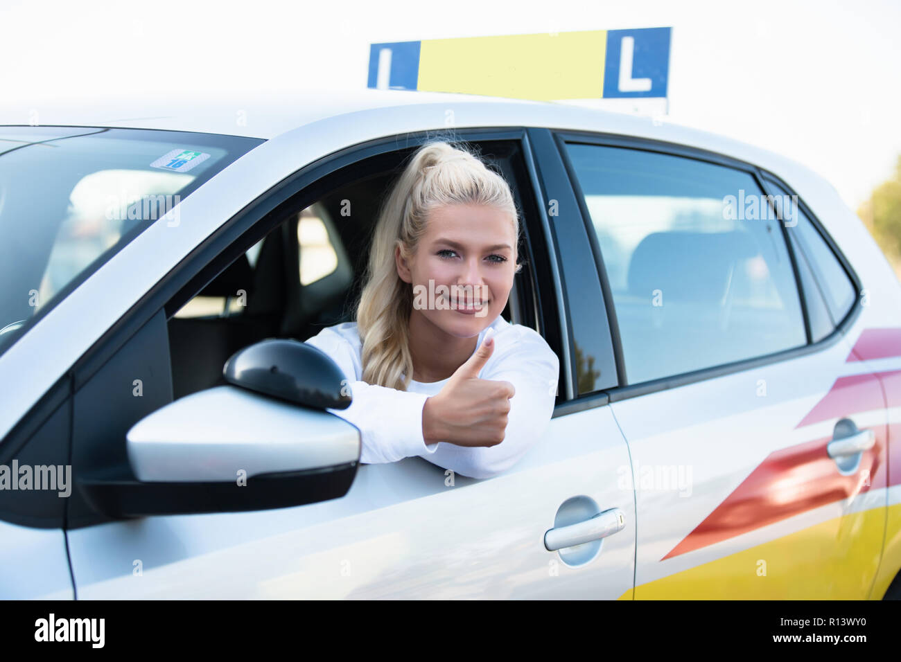 Driving school. Female young car driver going thumbs up after passing ...