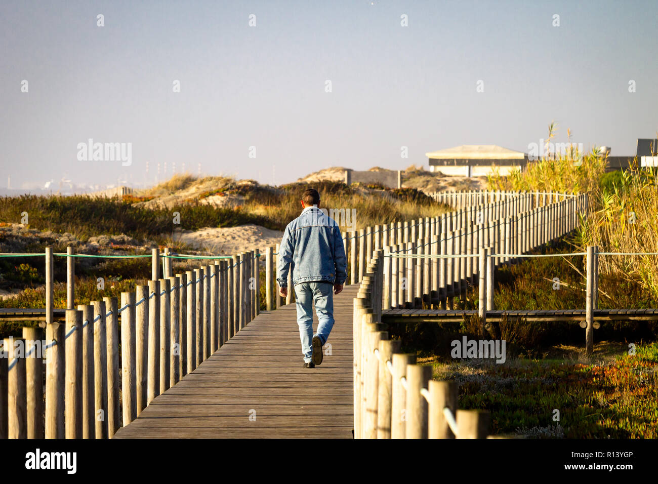 Man walks on boardwalk near the sand and the ocean. Denim. Back View ...
