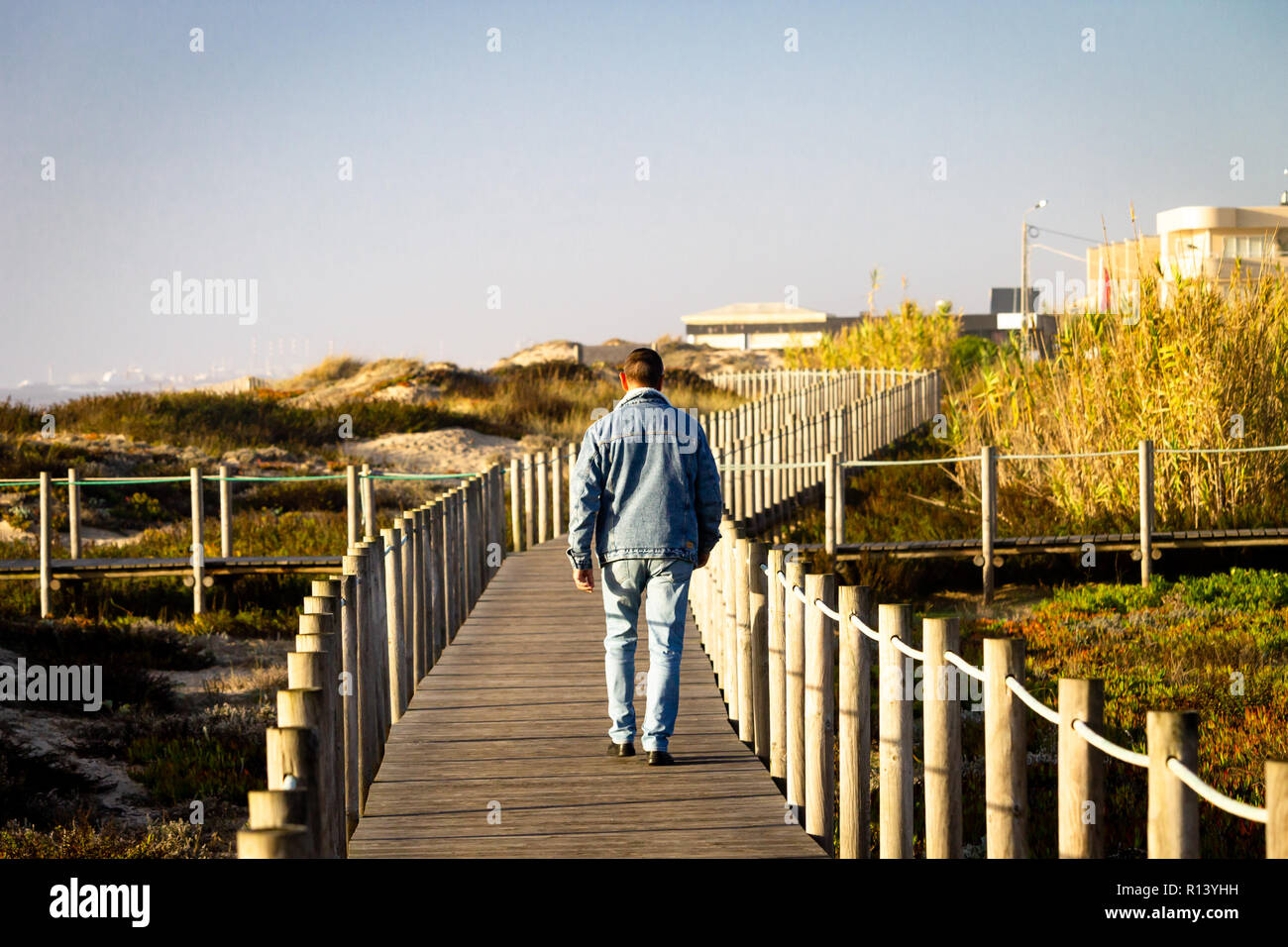 Man walks on boardwalk near the sand and the ocean. Denim. Back View ...