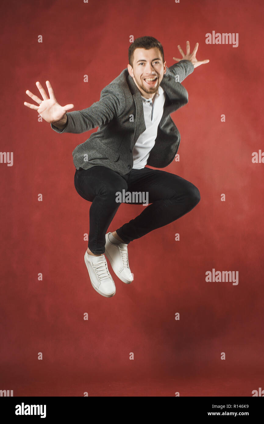 Photo of a young man on a red wall background looking at camera jumping ...