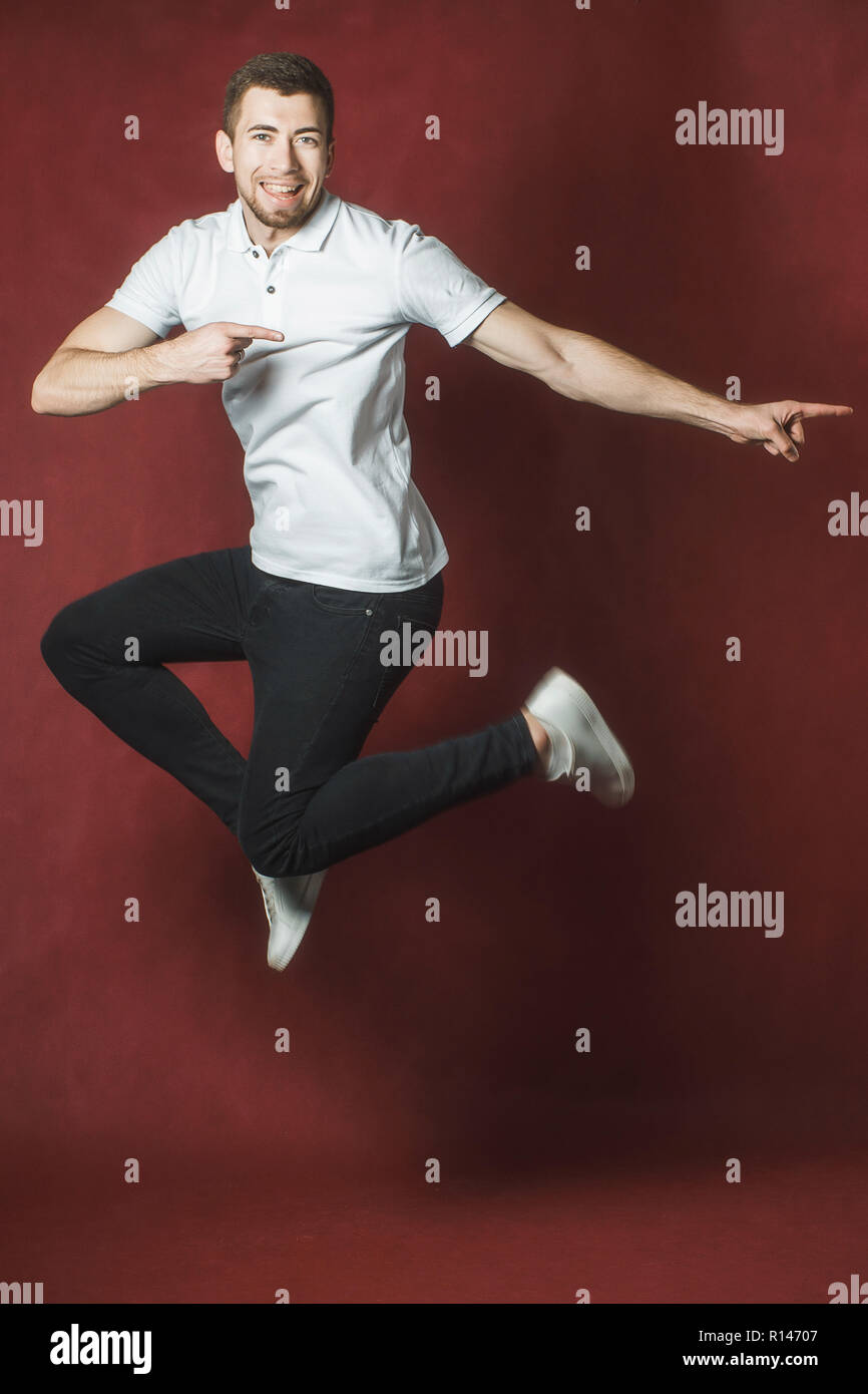 Photo of a young man on a red wall background looking at camera jumping ...