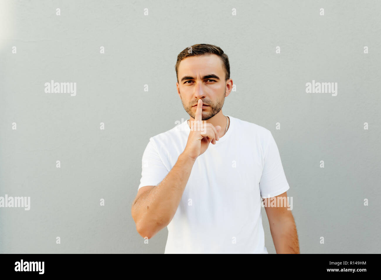 Shhh gesture. Young man isolated on gray background dressed in white ...