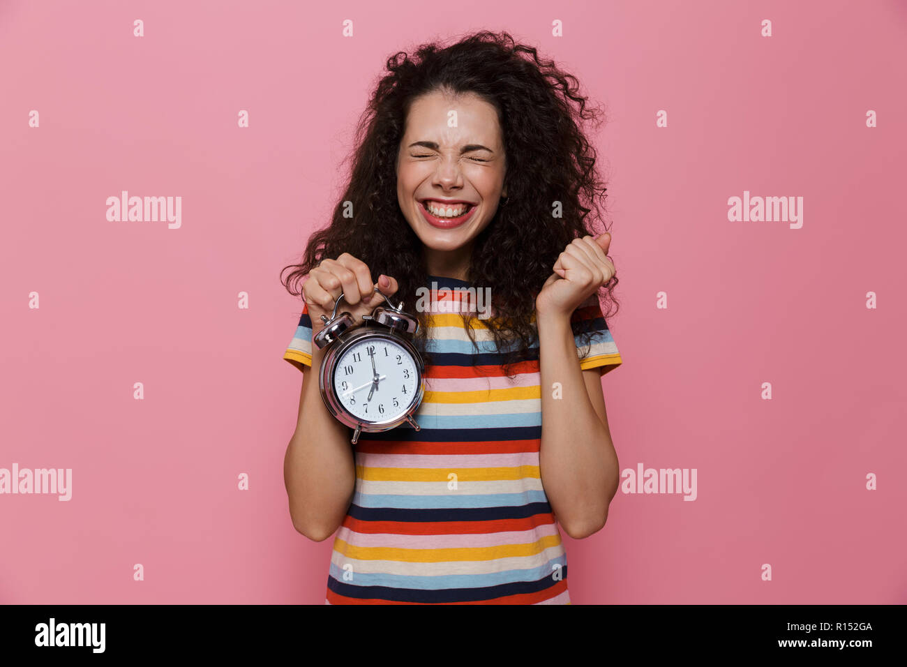 Photo of nervous woman 20s with curly hair holding alarm clock isolated ...
