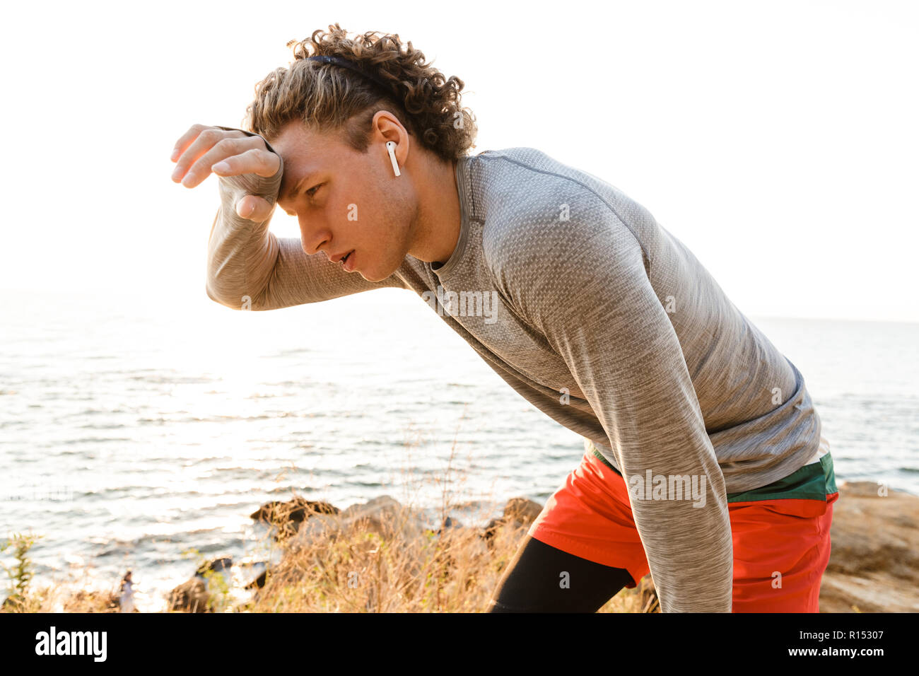 Photo of handsome tired young sports man standing on the beach have a ...