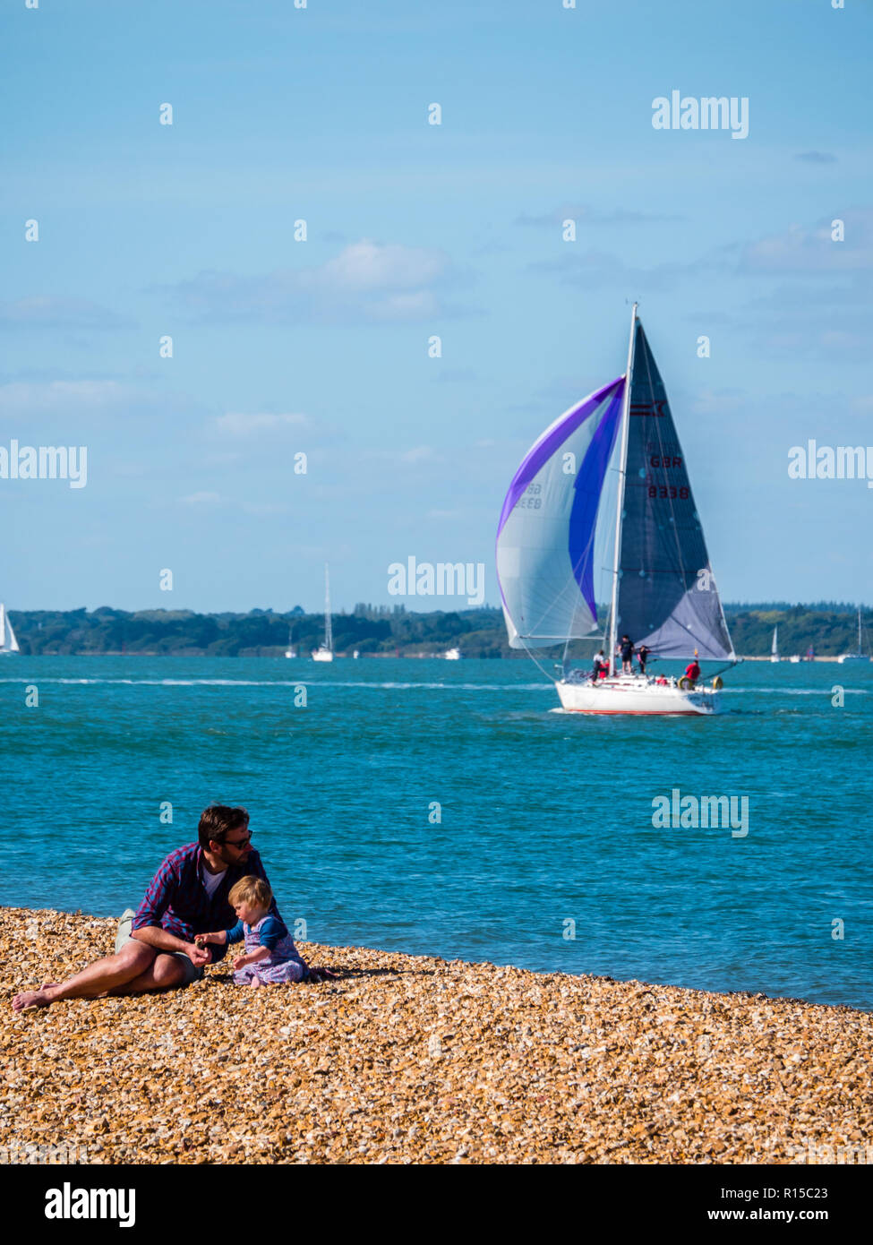 Father and Son Relaxing on Cowes, Pebble Beach, with Sailing Yacht on ...