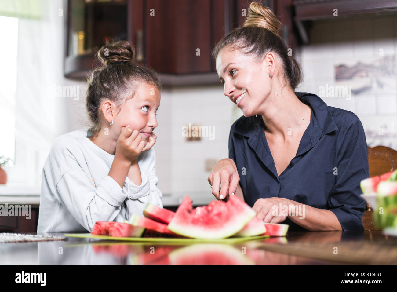 Cute little girl and her beautiful mom are cutting fruits and smiling ...