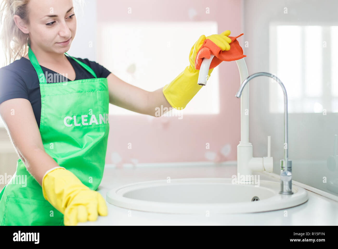 cleaning service. a young woman in an apron wipes dust with a rag Stock ...