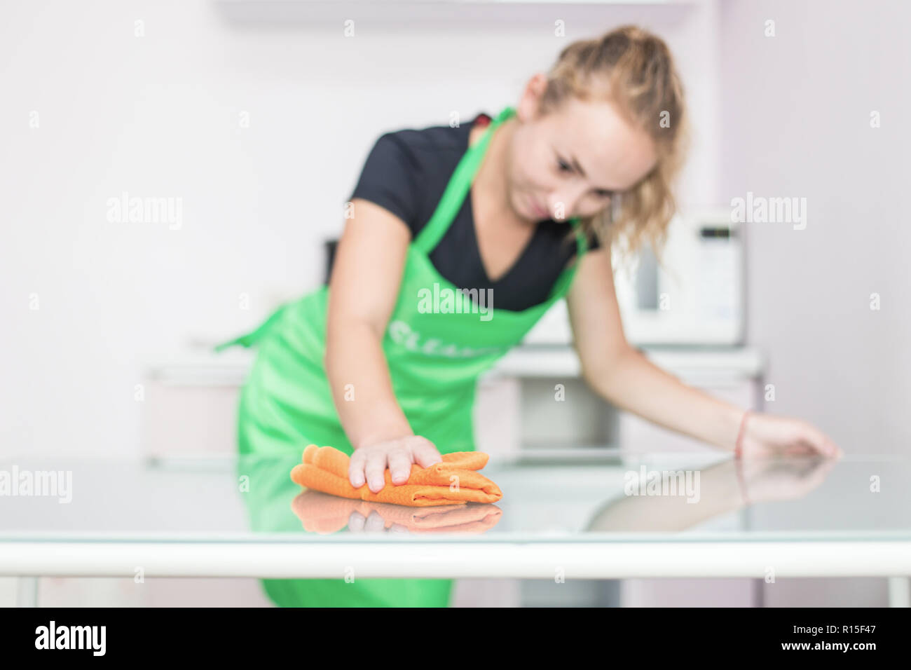 cleaning service. a young woman in an apron wipes dust with a rag Stock ...