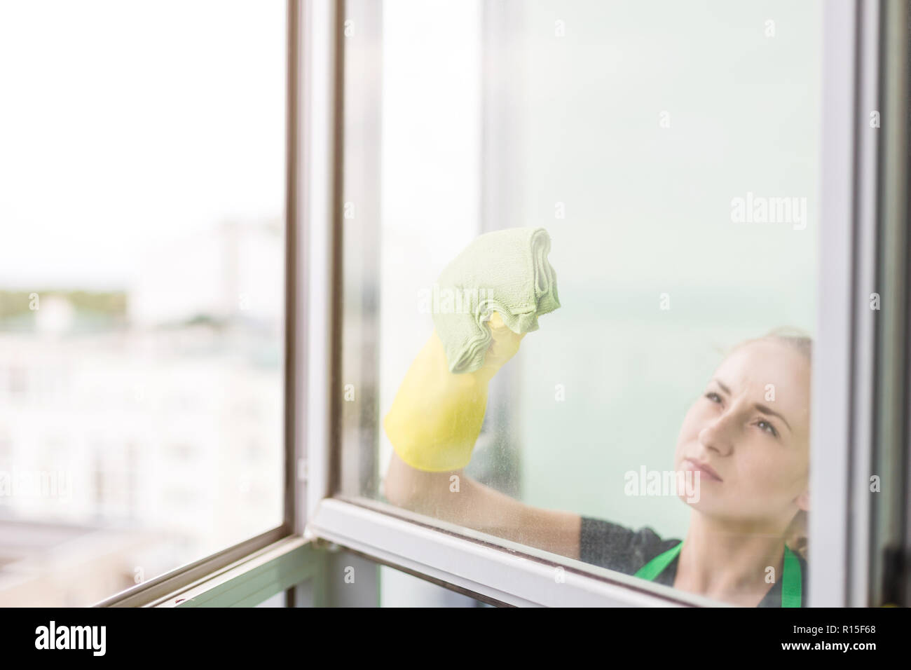 Smiling young woman worker cleaning soap suds on glass window with ...