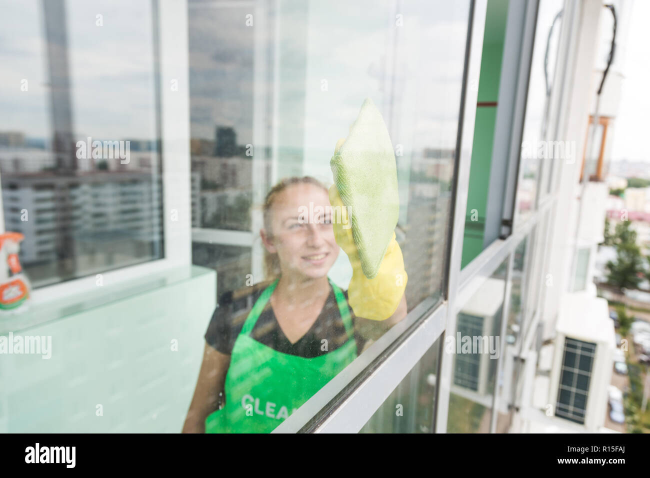 Smiling young woman worker cleaning soap suds on glass window with ...