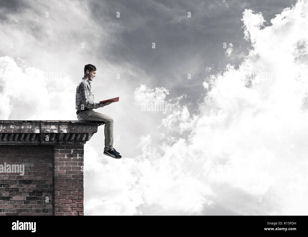Man on roof edge reading book and cloudscape at background Stock Photo ...