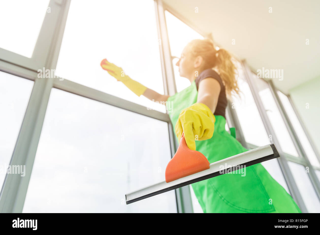 Smiling young woman worker cleaning soap suds on glass window with ...