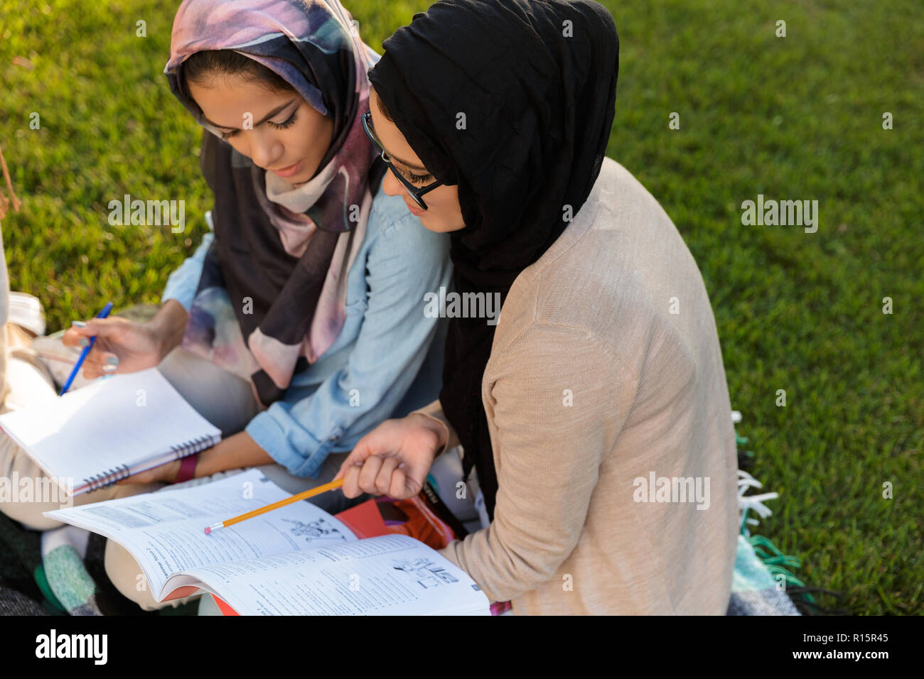 Photo of a young arabian women students writing in copybooks in park ...