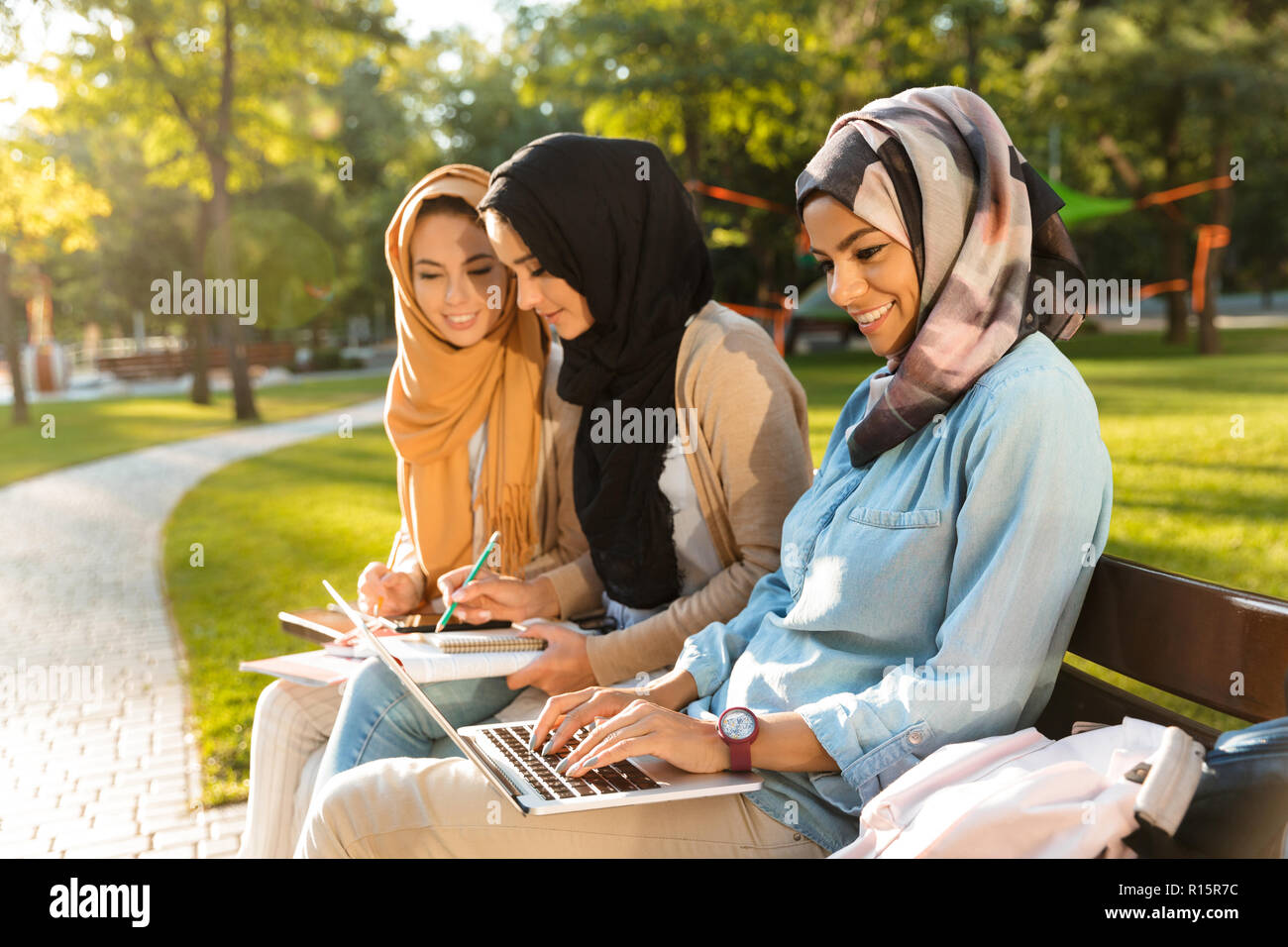 Group of three smiling muslim women students sitting on a bench ...