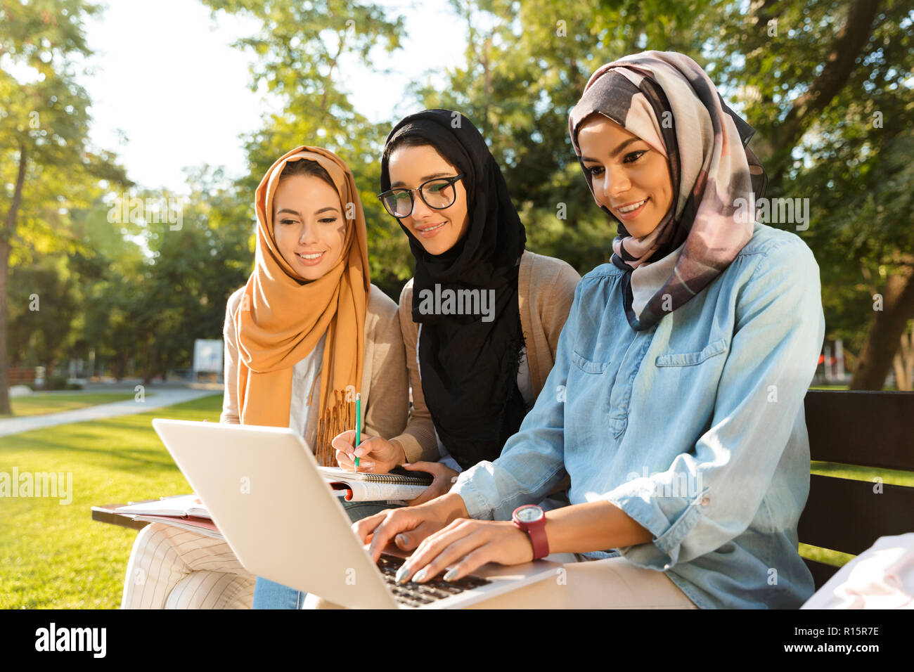 Group of three cheerful muslim women students sitting on a bench ...