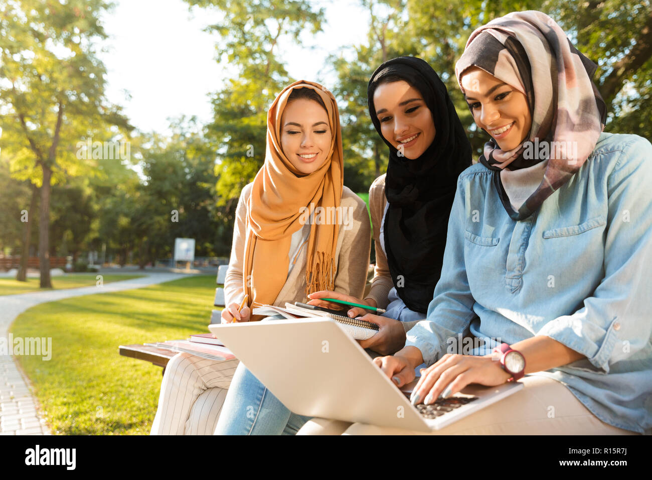Group of three happy muslim women students sitting on a bench outdoors ...