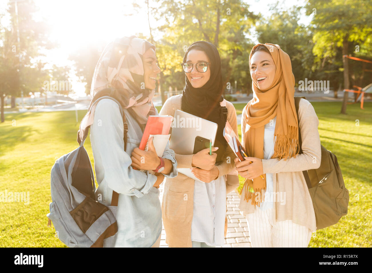 Group of three smiling muslim women students carrying backpacks and ...