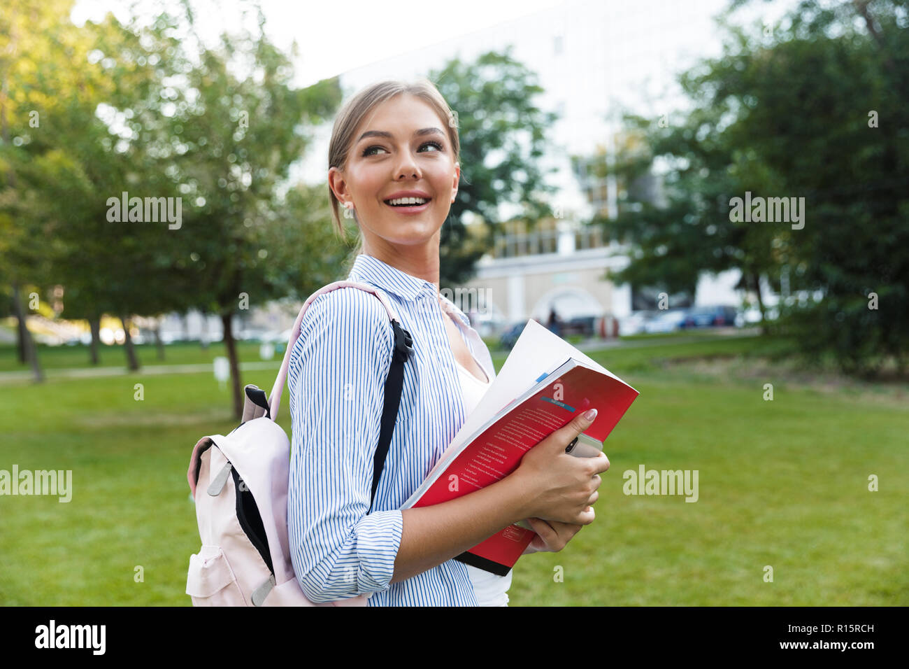 Cheerful young girl carrying backpack spending time at the park ...