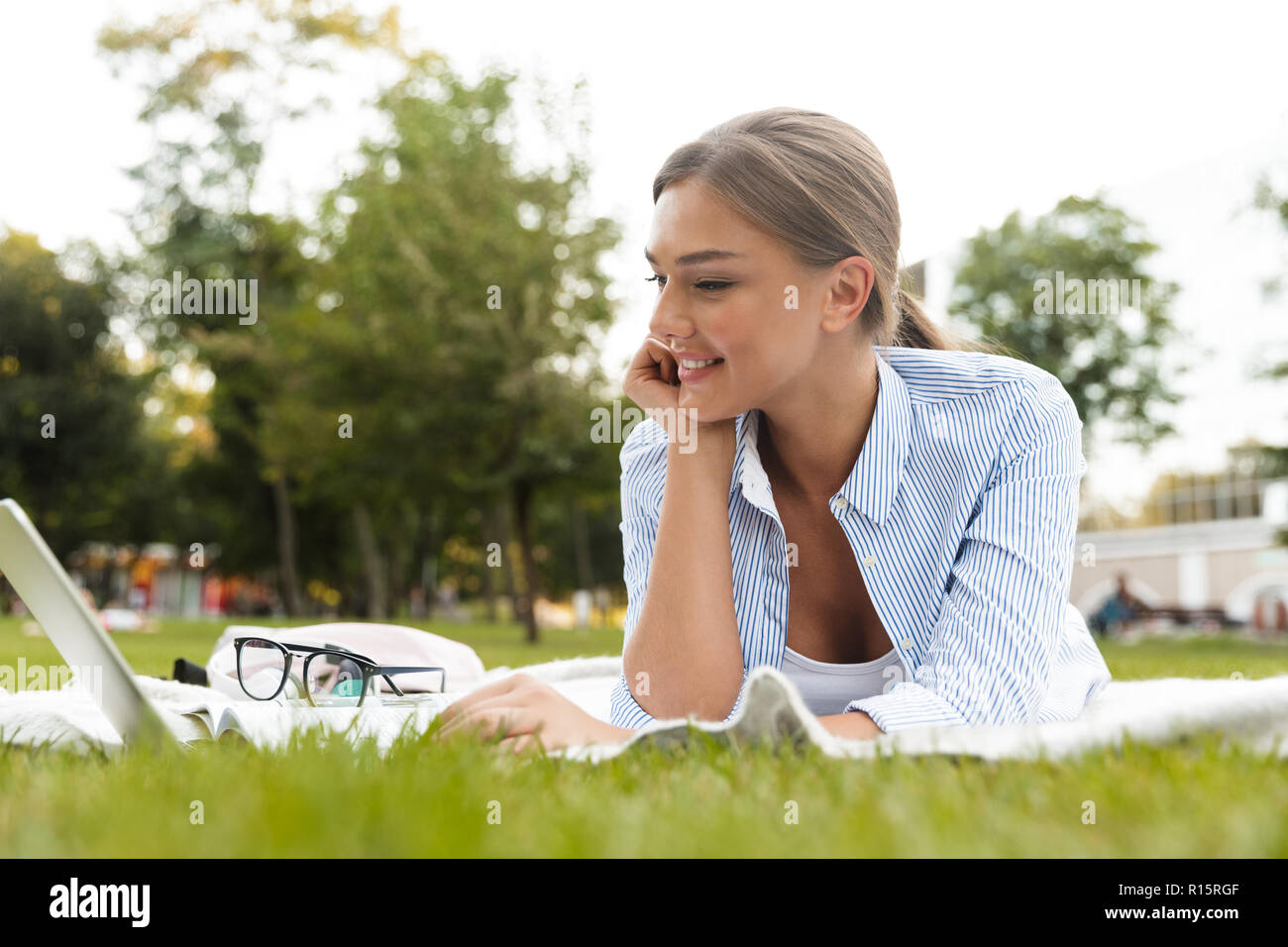 Lovely young girl spending time at the park, studying, laying on a ...