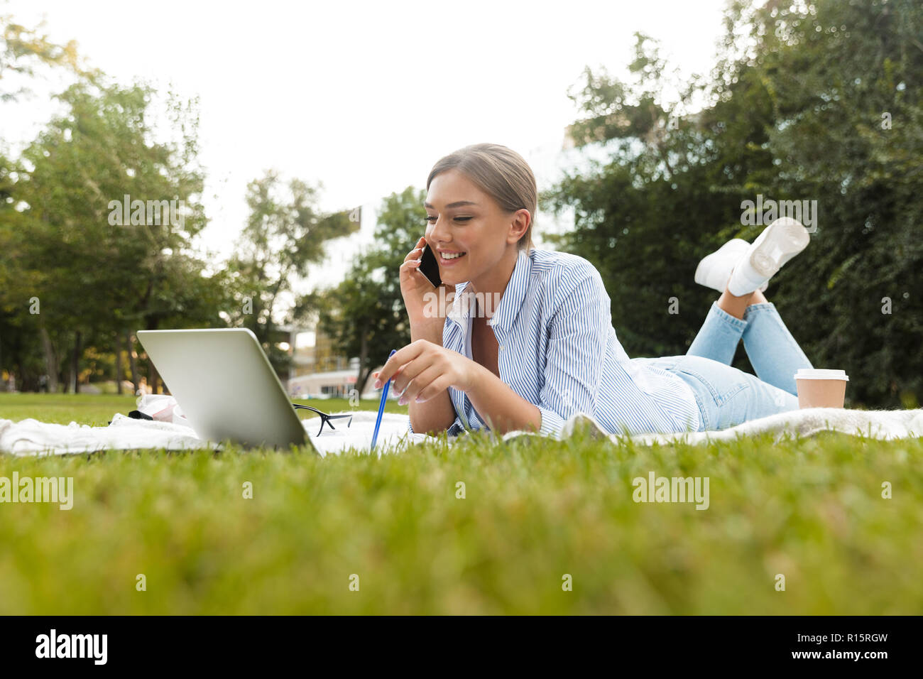 Smiling young girl spending time at the park, studying, laying on a ...