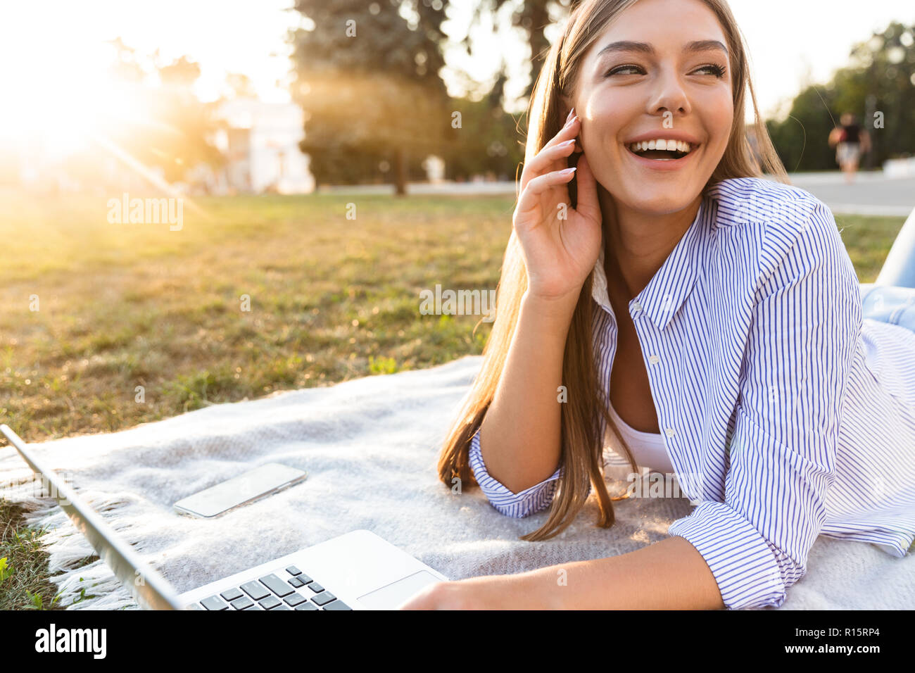 Cheerful young girl spending time at the park, studying, laying on a ...