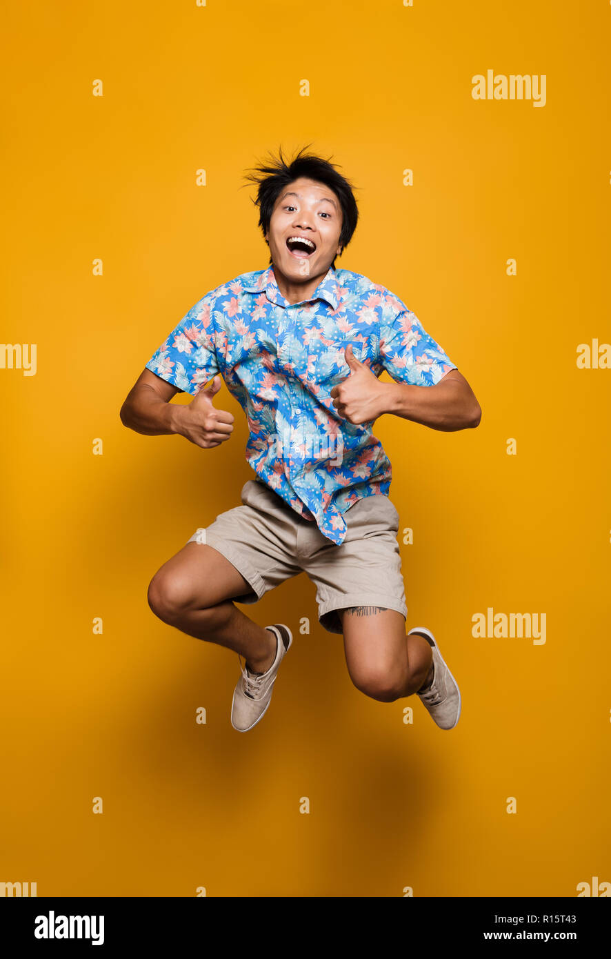 Image of happy emotional young asian man jumping isolated over yellow ...