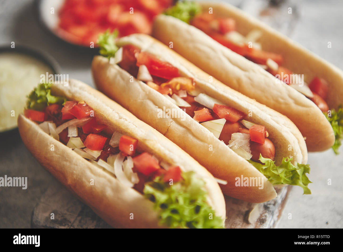 Three barbecue grilled hot dogs with sausage placed on wooden cutting ...