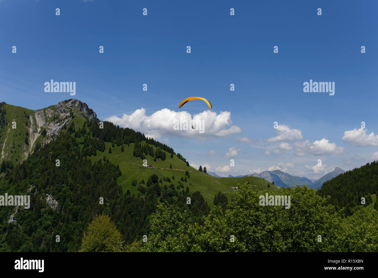 Yellow paragliderflying in blue skies and mountains above Lake Annecy ...