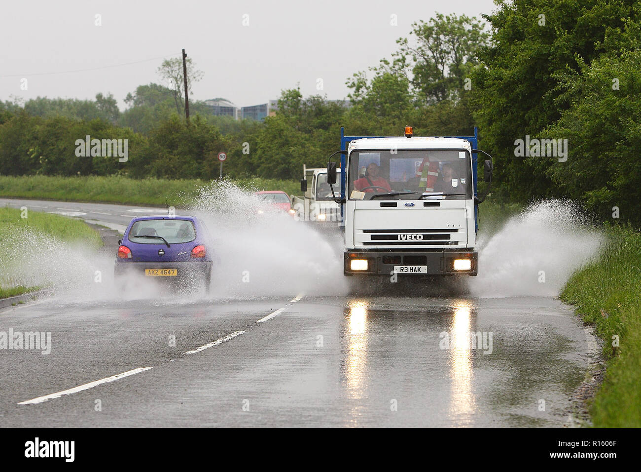 Cars and lorries being splashed by standing water on a road after ...