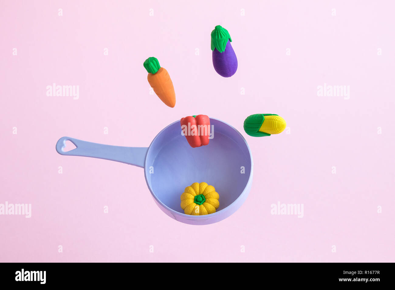 Pan with flying vegetable toys on pastel pink background minimal ...