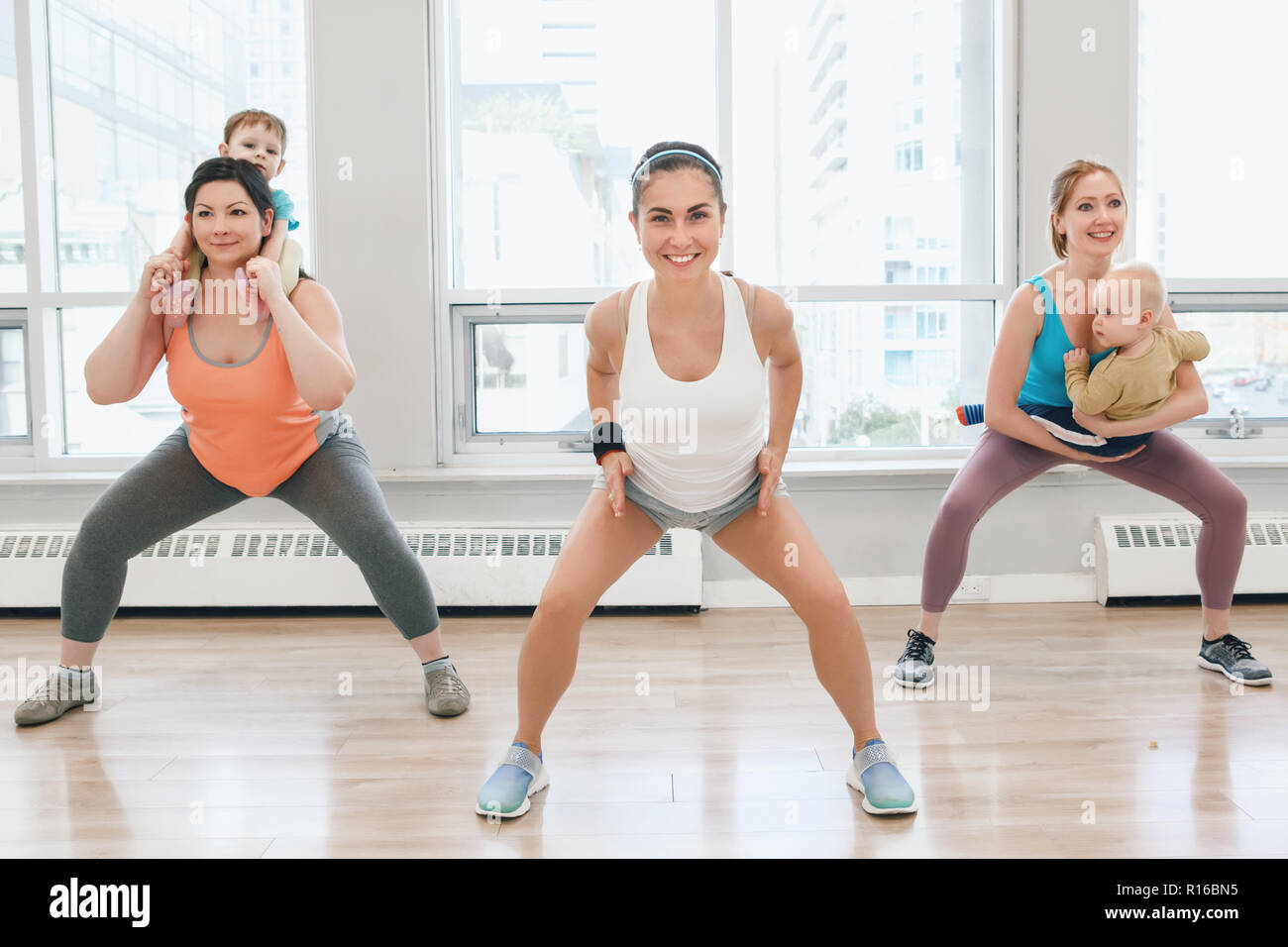 Group of three young women with children doing workout in gym class ...